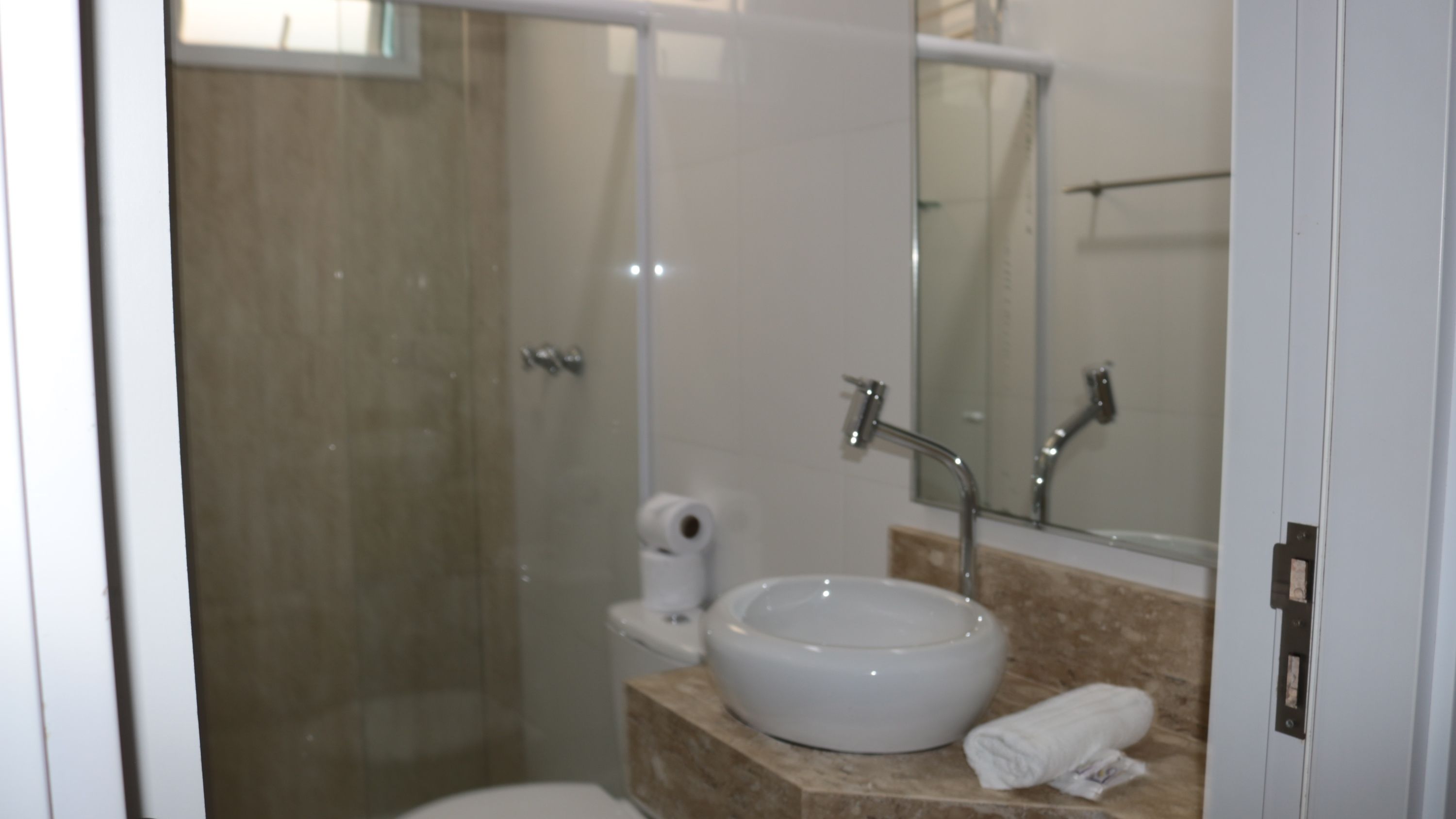 Uma casa de banho moderna com cabine de chuveiro em vidro, lavatório branco e bancada de mármore.