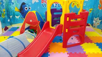 Espaço infantil com escorrega, estruturas de escalada e piso colorido.