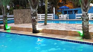 Piscina com borda de pedra, cercada por palmeiras e um muro branco.