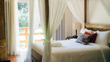 Quarto com cama de dossel, cabeceira de madeira e vista para o verde lá fora.