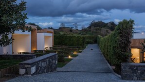 Uma trilha leva a um edifício moderno com paredes de pedra e detalhes em madeira.