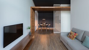 Uma sala de estar moderna com televisão de tela plana, um sofá cinza e um espaço de jantar com mesa e cadeiras.