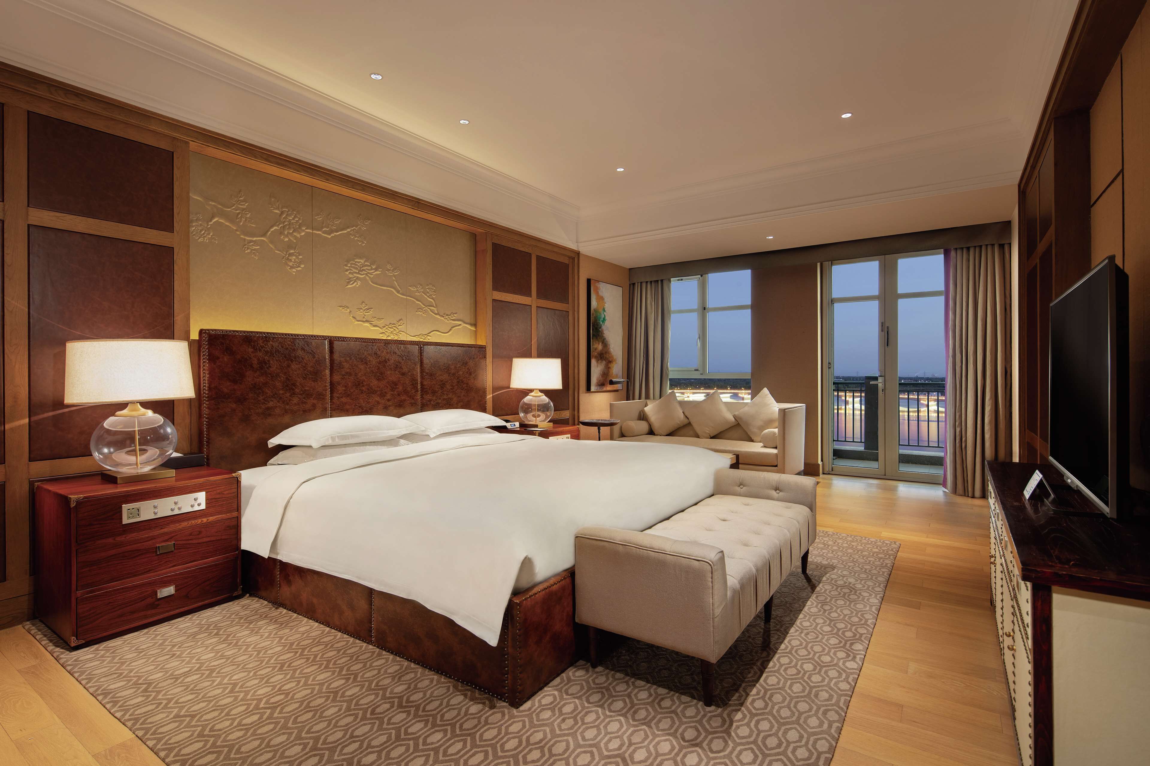 Quarto de hotel espaçoso com uma cama grande, um sofá, uma TV e uma varanda com vista.