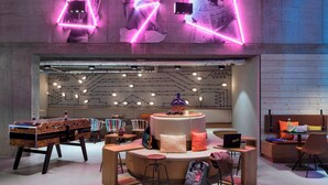 Uma área de lounge moderna com mesa de futebol, assentos e uma mesa central com um objeto decorativo.