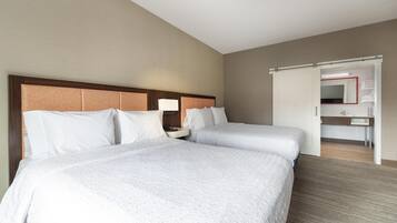 Quarto de hotel com duas camas, uma cabeceira de madeira, mesa de cabeceira com abajur e armário com espelho e prateleiras.