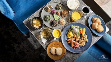 Buffet de café da manhã com diversos pratos, incluindo ovos, salsichas e doces, sobre uma mesa de mármore.