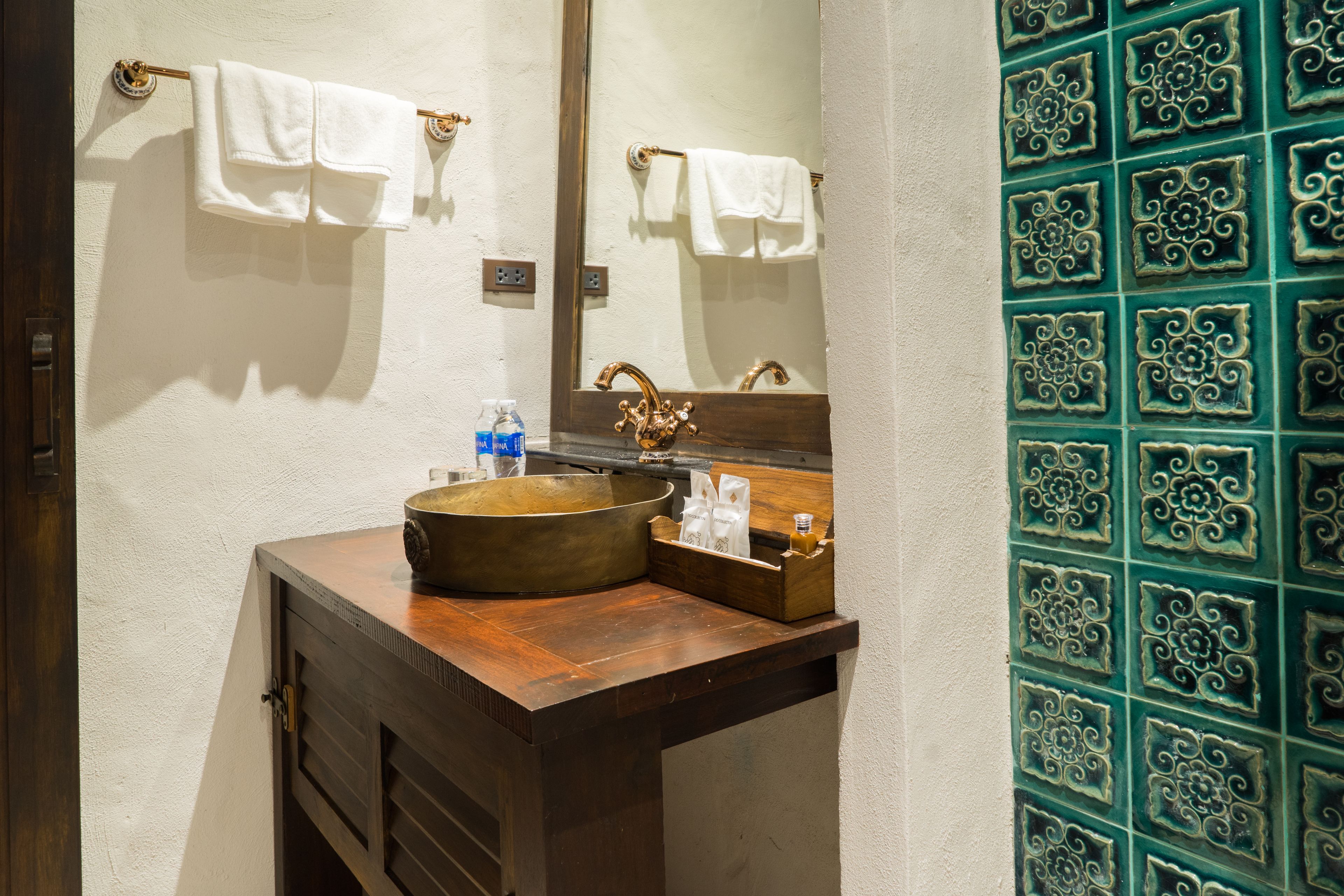 Um banheiro com toucador de madeira, uma pia grande e um espelho sobre ela. Toalhas penduradas em um porta-toalhas e uma parede com azulejos decorativos.