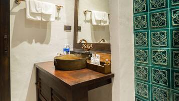 Um banheiro com toucador de madeira, uma pia grande e um espelho sobre ela. Toalhas penduradas em um porta-toalhas e uma parede com azulejos decorativos.