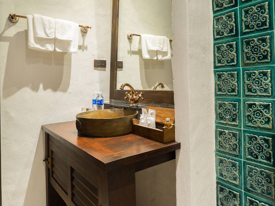 Um banheiro com toucador de madeira, uma pia grande e um espelho sobre ela. Toalhas penduradas em um porta-toalhas e uma parede com azulejos decorativos.
