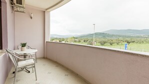 Uma varanda com mesa e cadeiras, um vaso de planta e vista para colinas ao longe.