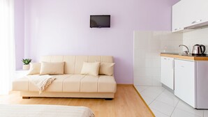 Quarto moderno com sofá, pequena cozinha e televisão na parede.