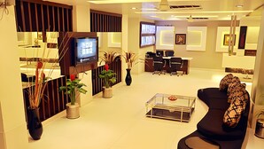 Uma sala de estar moderna com um sofá preto, uma TV e um espaço de trabalho com cadeiras.