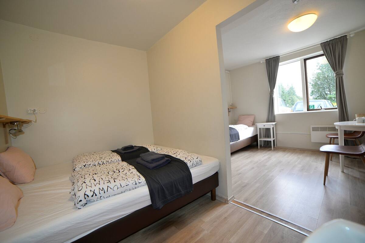 Quarto com cama, mesa de cabeceira e janela com cortinas.