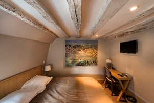 Um quarto com uma cama, uma escrivaninha, uma cadeira, um quadro e uma televisão na parede.