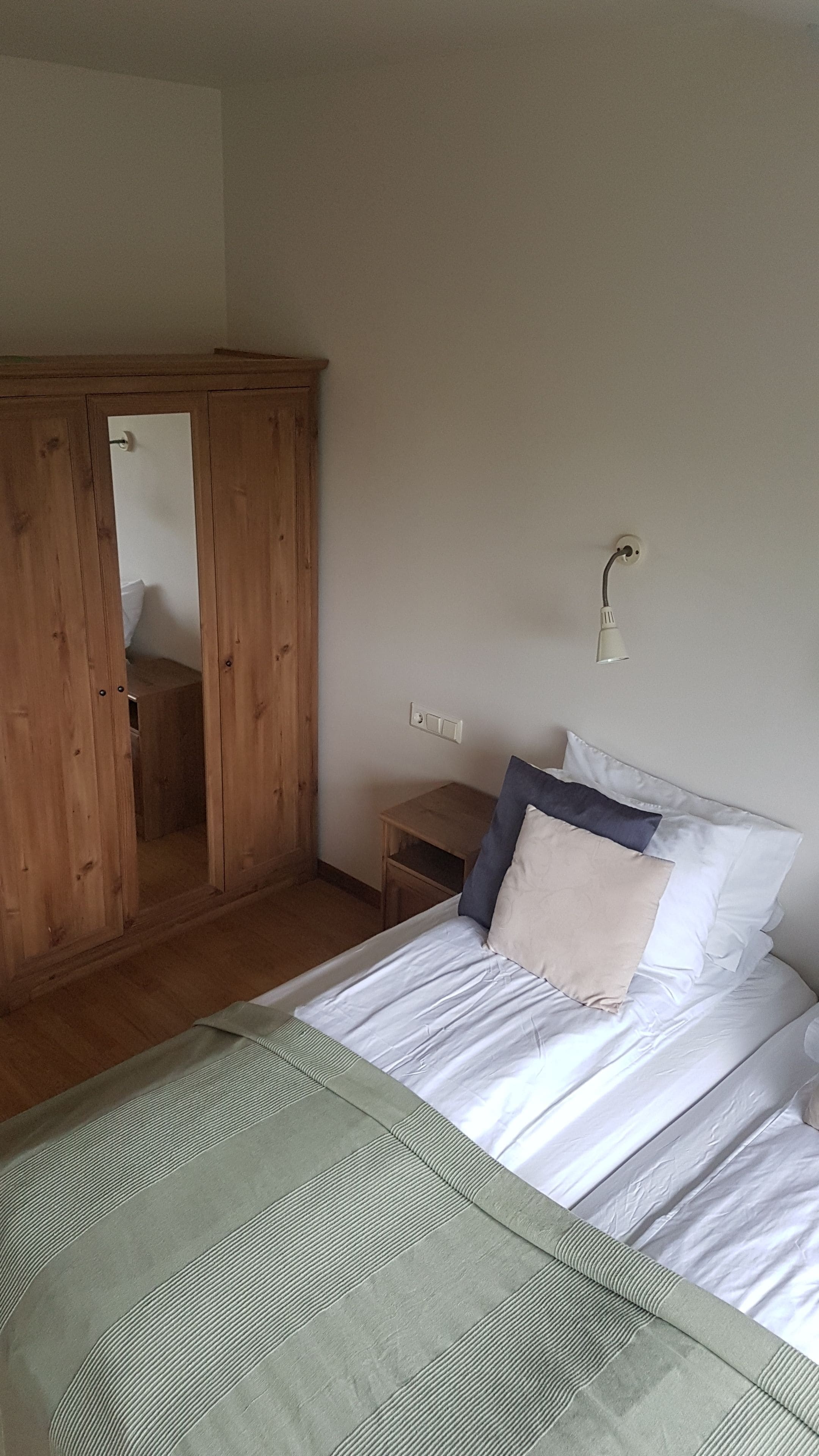 Quarto com cama, guarda-roupa de madeira, mesa de cabeceira e luminária na parede.