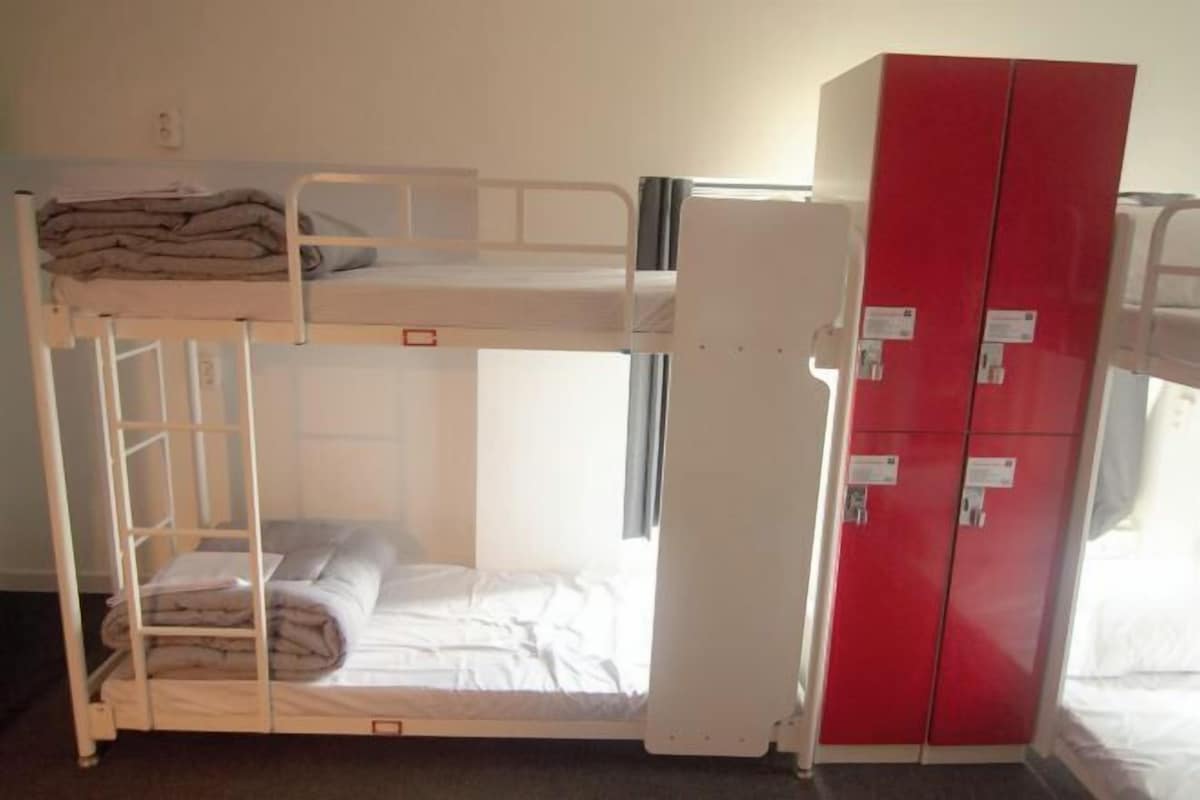 Quarto com beliche, guarda-roupa vermelho e frigorífico branco.
