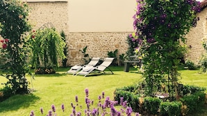 Um jardim com gramado, duas espreguiçadeiras e um muro de pedra.