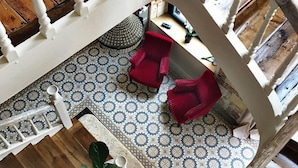 Um quarto com pé-direito alto, piso estampado, escada e cadeiras vermelhas.