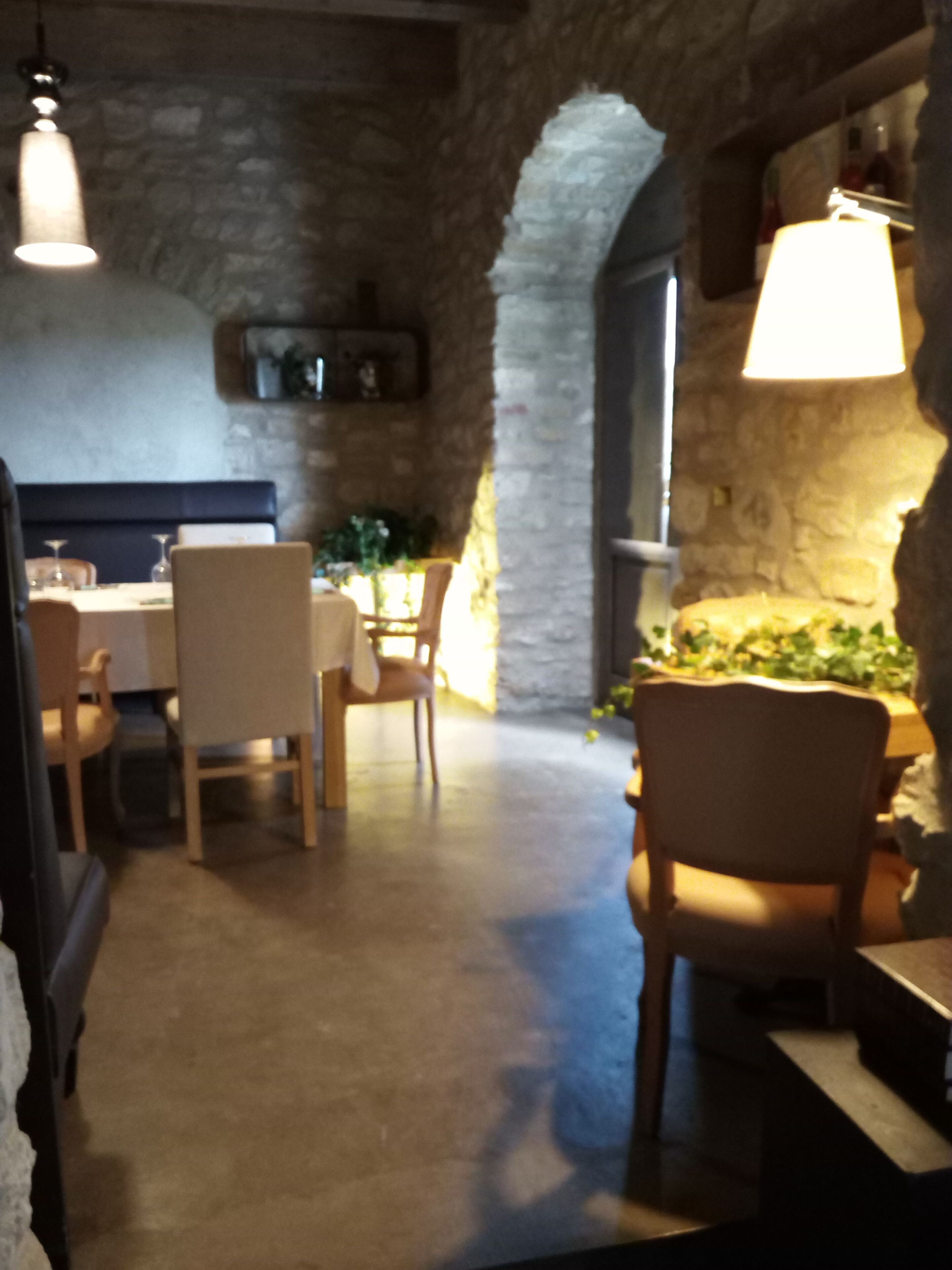 Uma sala de jantar com paredes de pedra, mesa posta para dois, cadeiras e luminárias pendentes.