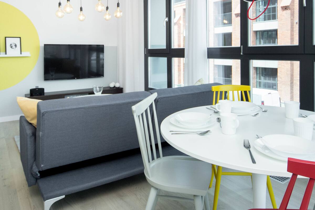 Uma sala de jantar moderna com uma mesa redonda, cadeiras brancas e um sofá cinzento.
