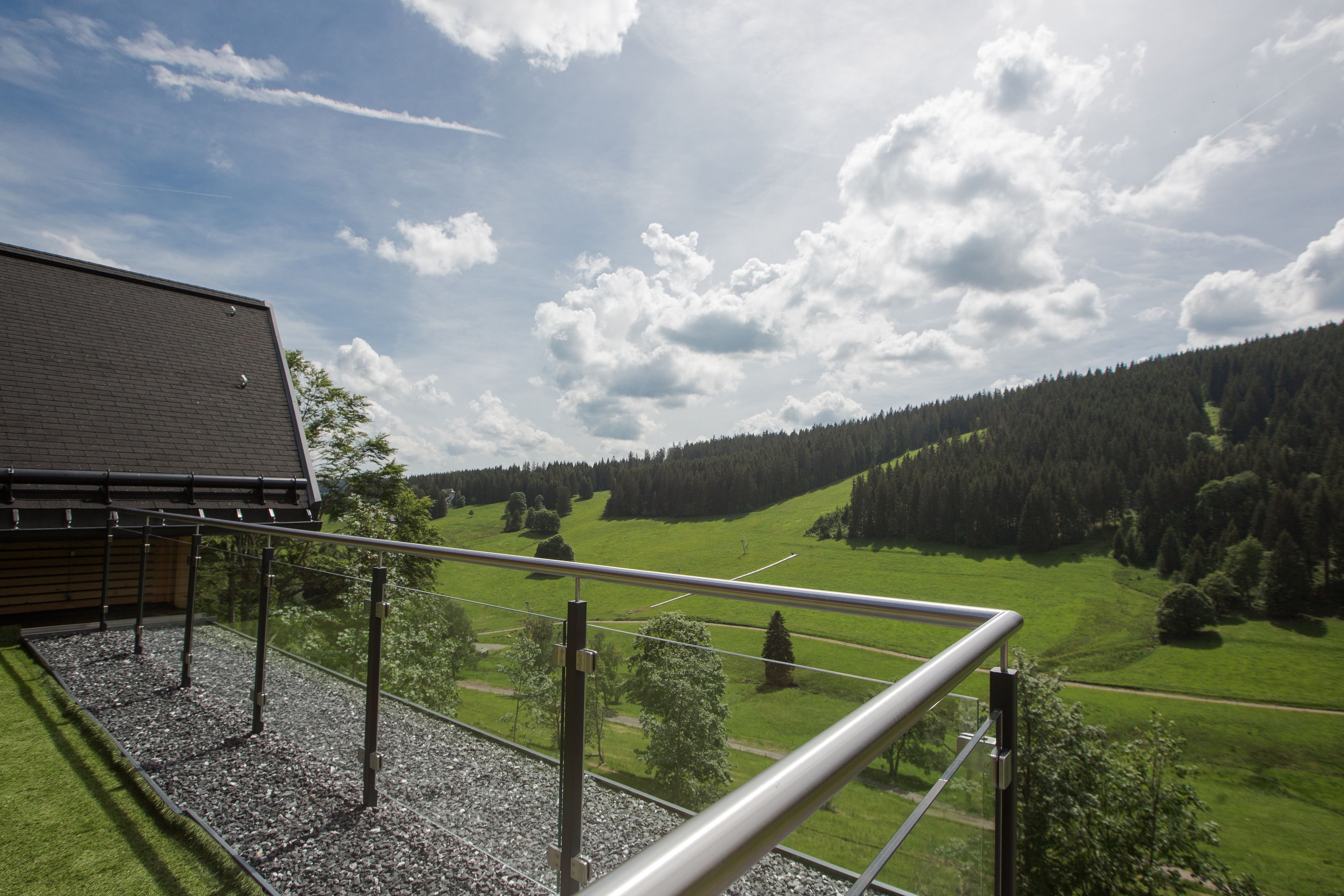 Uma varanda com guarda-corrimão de metal, com vista para uma paisagem verde com árvores e um edifício ao fundo.