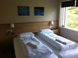 Quarto de hotel com duas camas de solteiro, cabeceira de madeira, duas luminárias fixadas na parede e dois quadros emoldurados.
