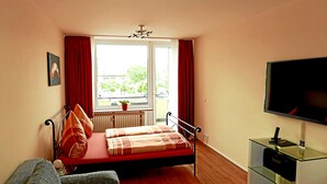 Quarto com cama, televisão, radiador, janela com cortinas e vista para o exterior.