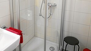 Um chuveiro com porta de vidro, uma pia branca e uma toalha vermelha.
