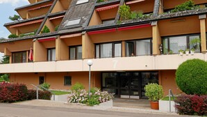 Hotel com vários andares, varandas, entrada no nível da rua e plantas em vasos.