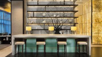Uma área de bar moderna com ilha central, banquetas e uma parede decorativa com tema de árvore.