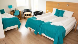 Quarto de hotel com duas camas de solteiro, uma escrivaninha com cadeira, uma mesinha redonda e uma janela.