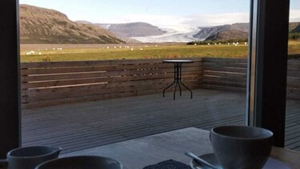 Quarto com vista para uma paisagem montanhosa e um pequeno espaço ao ar livre com mesa e cadeiras.