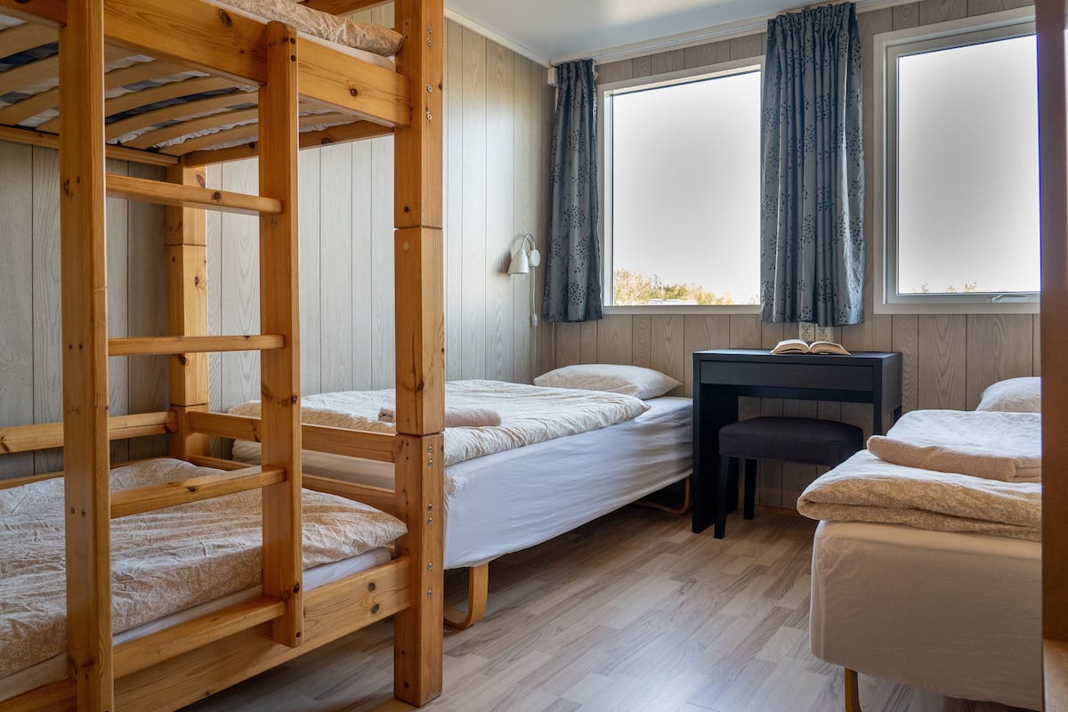 Um quarto de dormitório com beliches, uma escrivaninha e uma janela com cortinas.