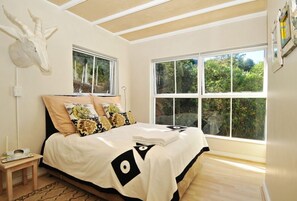 Quarto com cama, duas janelas, cabeça de animal montada e uma pequena mesa de cabeceira.
