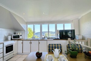 Cozinha com armários brancos, micro-ondas, fogão e televisão. Há uma janela com vista para o exterior.
