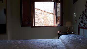 Quarto com cama, mesa de cabeceira, luminária e janela com persiana aberta.