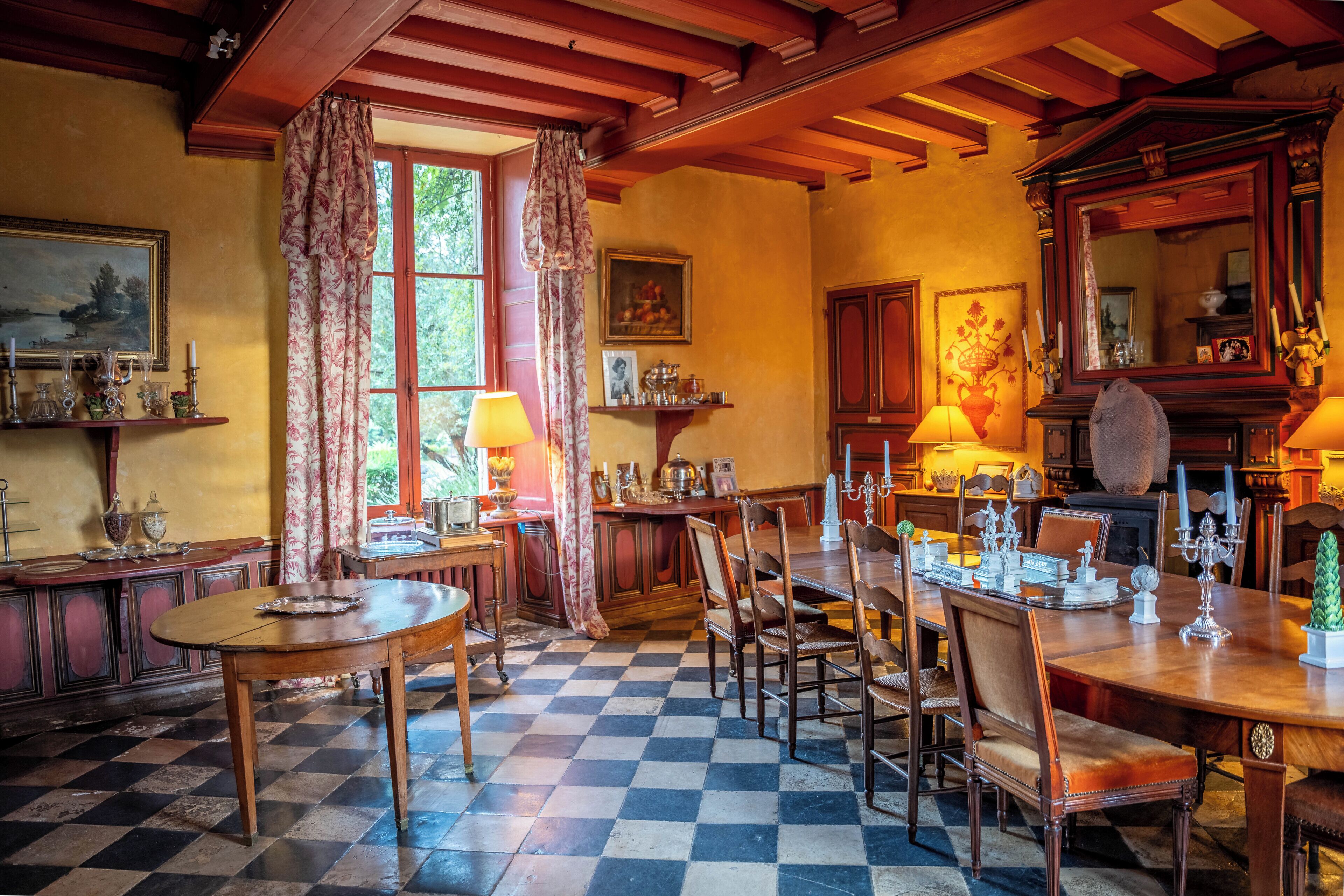 Uma sala de jantar com piso xadrez, móveis de madeira e diversos objetos decorativos.