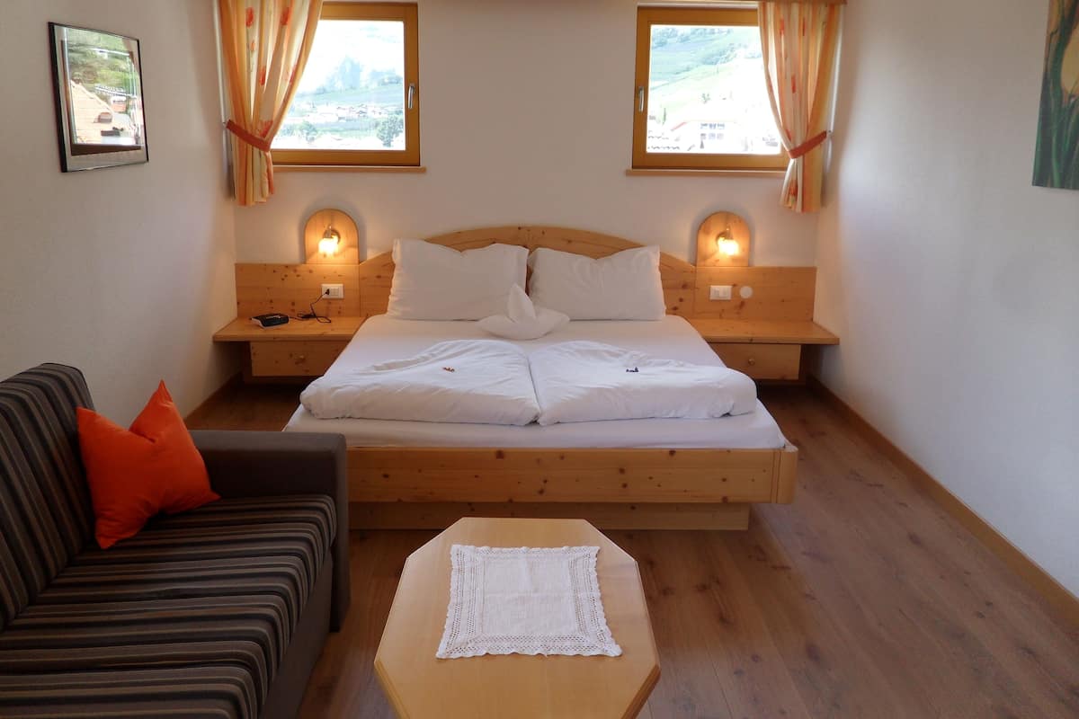 Quarto com cama de madeira, duas mesas de cabeceira com luminárias, um sofá listrado e uma pequena mesa com toalha branca.