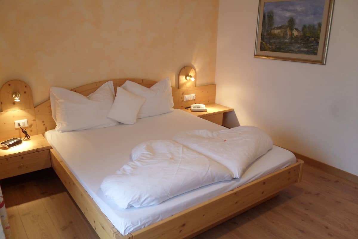 Uma cama bem arrumada com lençóis e almofadas brancas, cabeceira de madeira, luminárias de cabeceira e um quadro na parede.