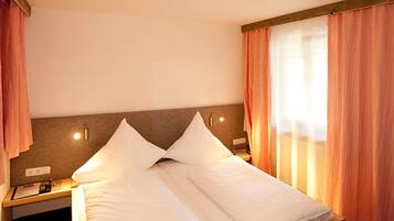 Quarto de hotel com cama, mesas de cabeceira, abajur e cortinas.