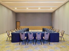Sala de conferência com uma mesa comprida, cadeiras e tela de projeção.
