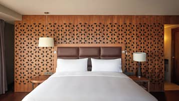 Quarto de hotel com uma cama grande, cabeceira de madeira, duas luminárias laterais e parede estampada.