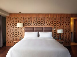 Quarto de hotel com uma cama grande, cabeceira de madeira, duas luminárias laterais e parede estampada.