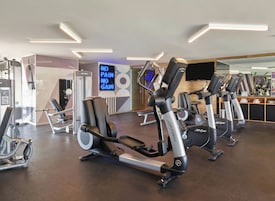 Uma academia com equipamentos de cardio, espelho e uma placa neon.