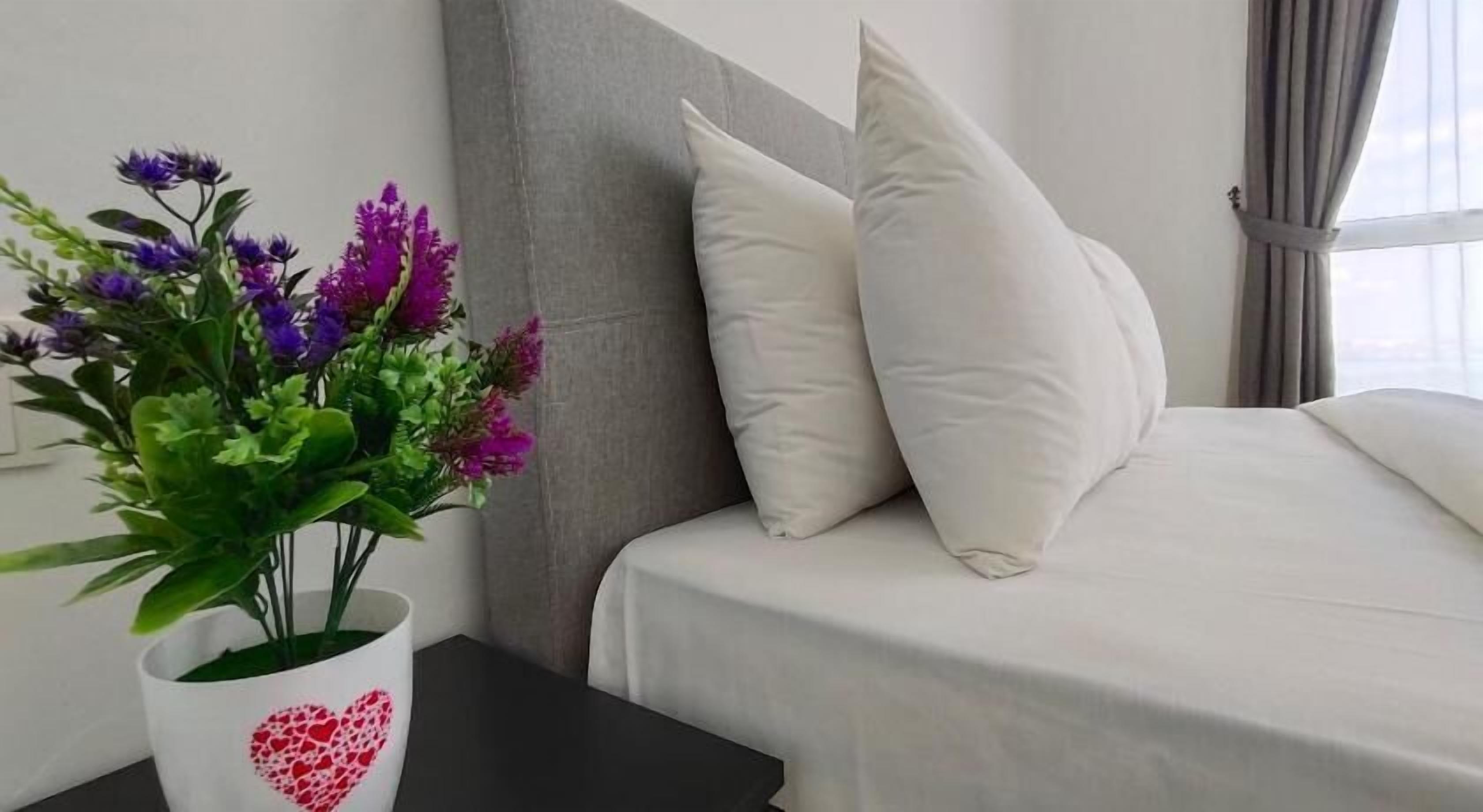 Quarto de hotel com cama, almofadas, mesa de cabeceira e um vaso de flores.