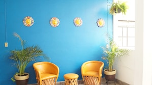 Quarto com parede azul, três cadeiras de vime, duas plantas em vasos e detalhes com motivos de sol.