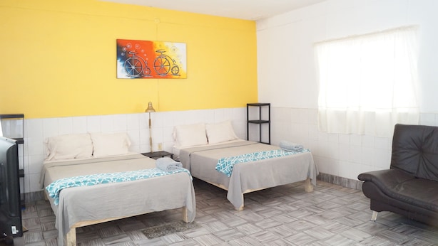 Quarto com duas camas, um sofá, um quadro na parede e uma janela com cortinas.