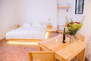 Quarto de hotel com cama, uma mesa de madeira com cadeiras, um vaso de flores e uma garrafa de vinho.