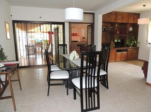 Uma área de jantar com mesa de vidro, cadeiras pretas e uma luminária pendente branca.