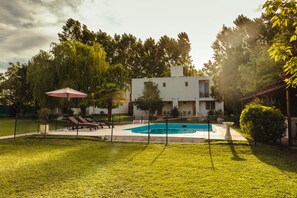 Uma casa moderna com piscina, cercada por um gramado bem cuidado e árvores.